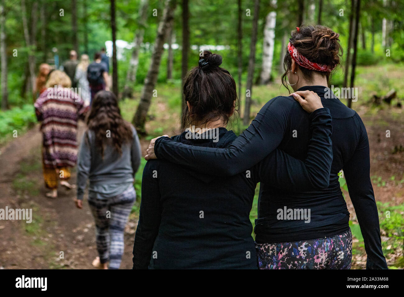 Two women support each other arm in arm, as they hike a forest trail ...