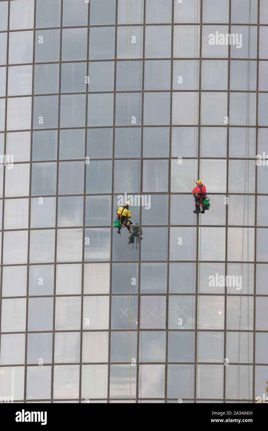 Two men workers hanging on ropes by the exterior windows of a ...