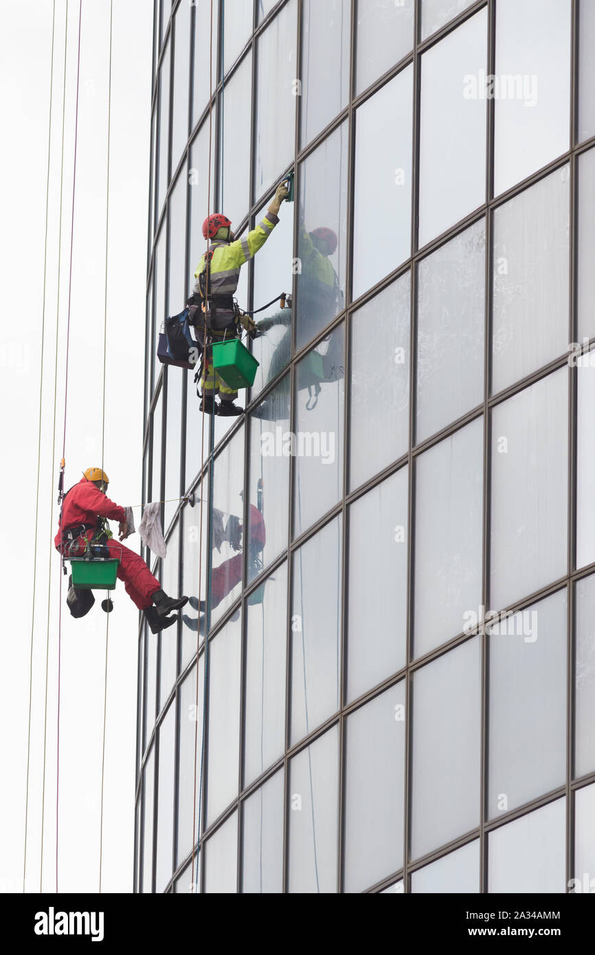 Two men workers hanging on ropes by the exterior windows of a ...