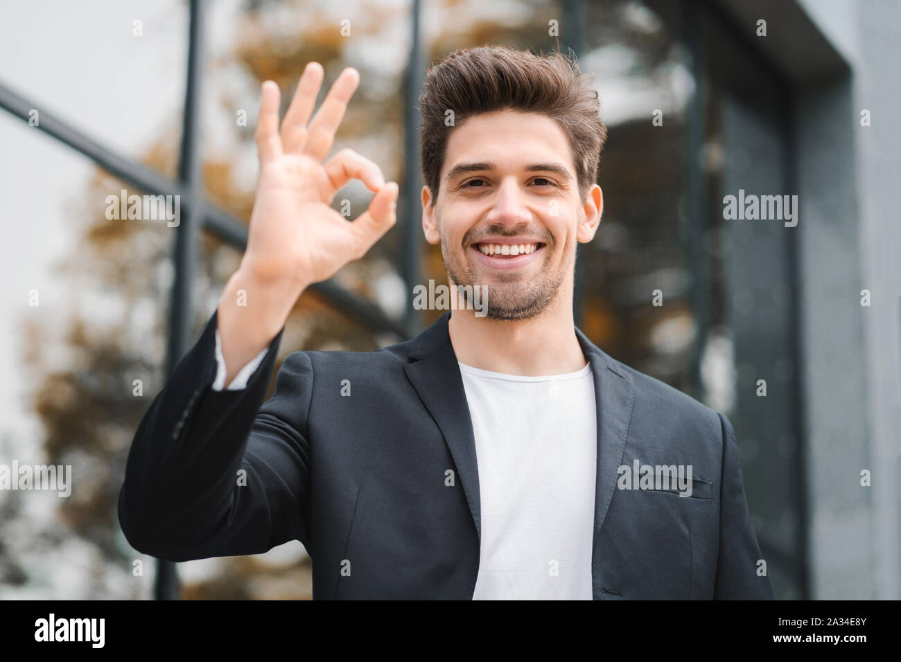 Successful man looking to camera and showing OK sign office building ...
