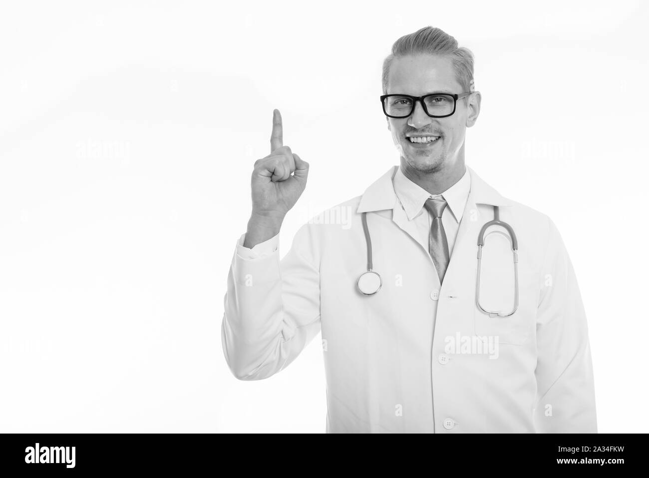 Studio shot of young happy man doctor smiling while pointing finger up ...
