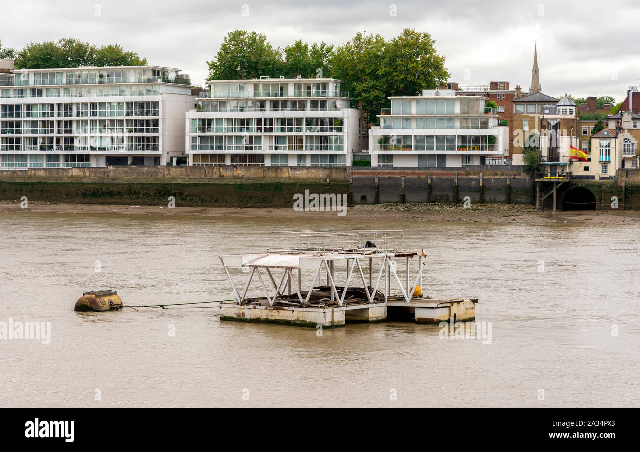 A small rusty floating pier in dirty waters of river Thames in front ...