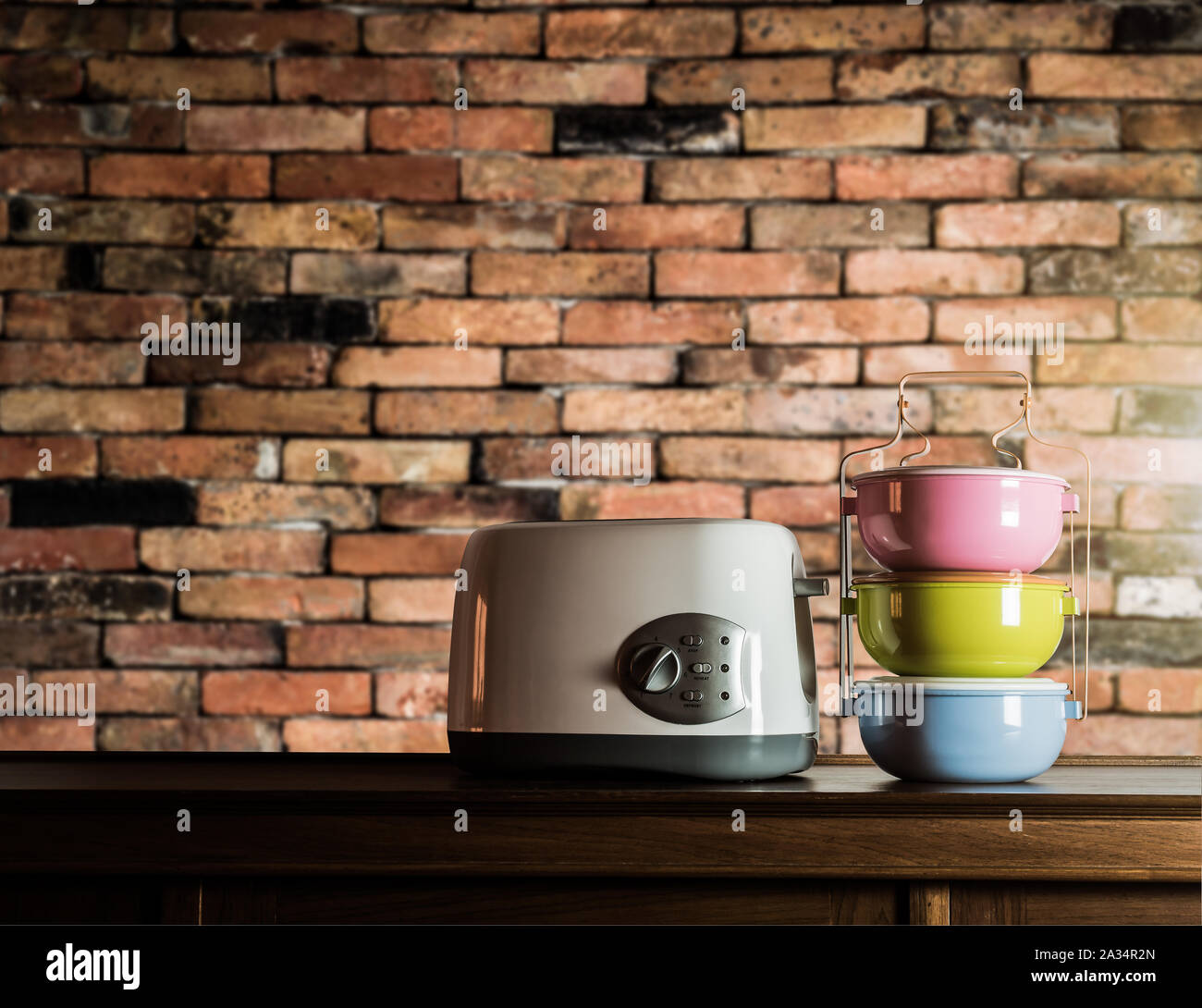 Colorful tiffin carrier and toaster on wooden cupboard with old brick ...