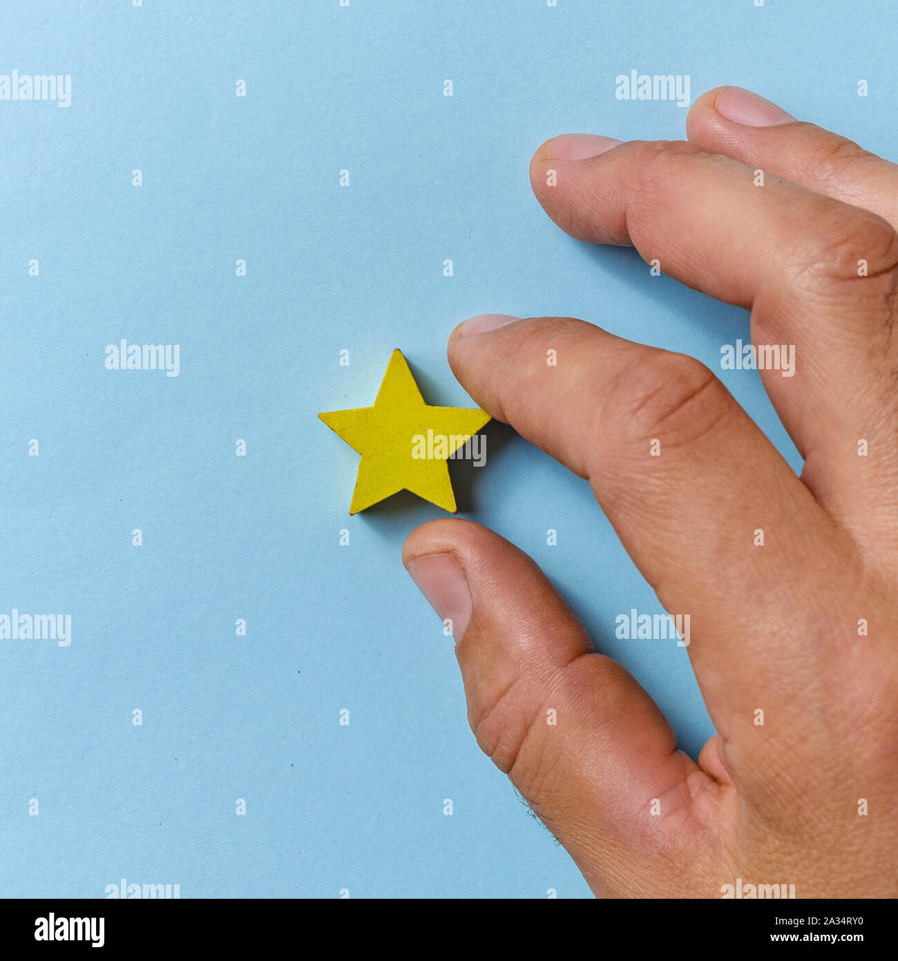 Male hand touching a single gold star over a square blue background ...