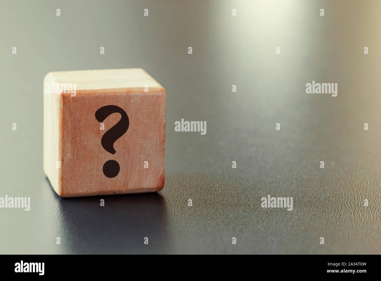 Small wooden toy block with question mark over a grey background with ...