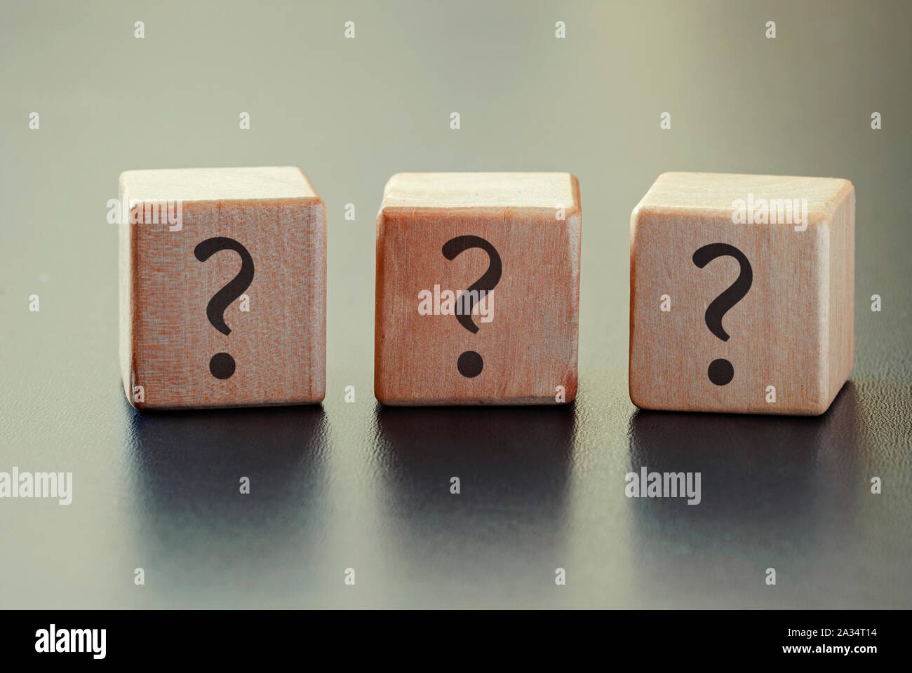 Three question marks on a row of small wooden blocks or cubes over grey ...
