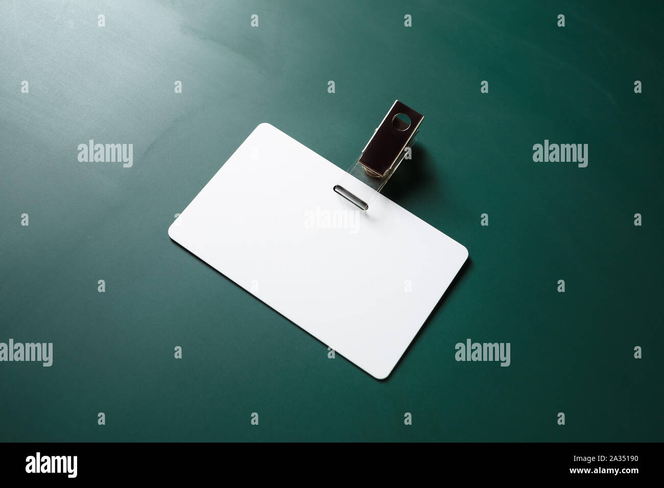 Blank white plastic badge on green chalkboard background. Empty ID card ...