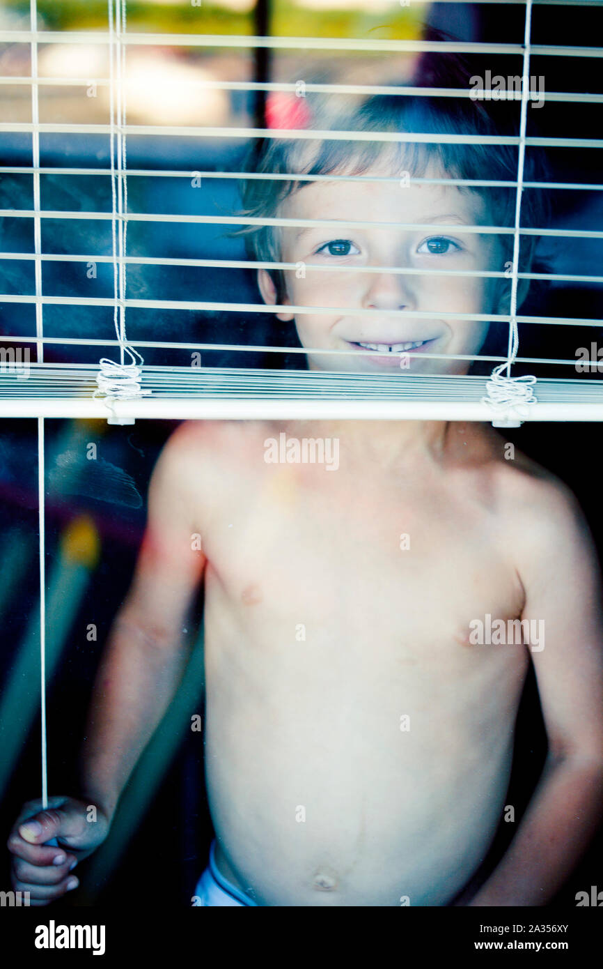 Little cute boy throught window making funny faces, home alone ...