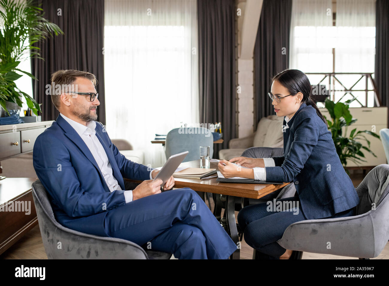 Two confident colleagues in formalwear discussing working moments at ...