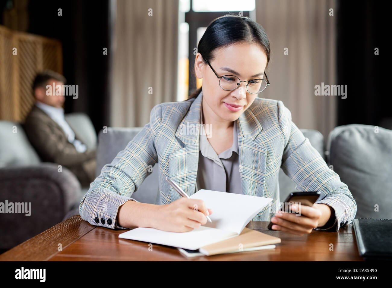 Young elegant businesswoman scrolling in smartphone while making ...