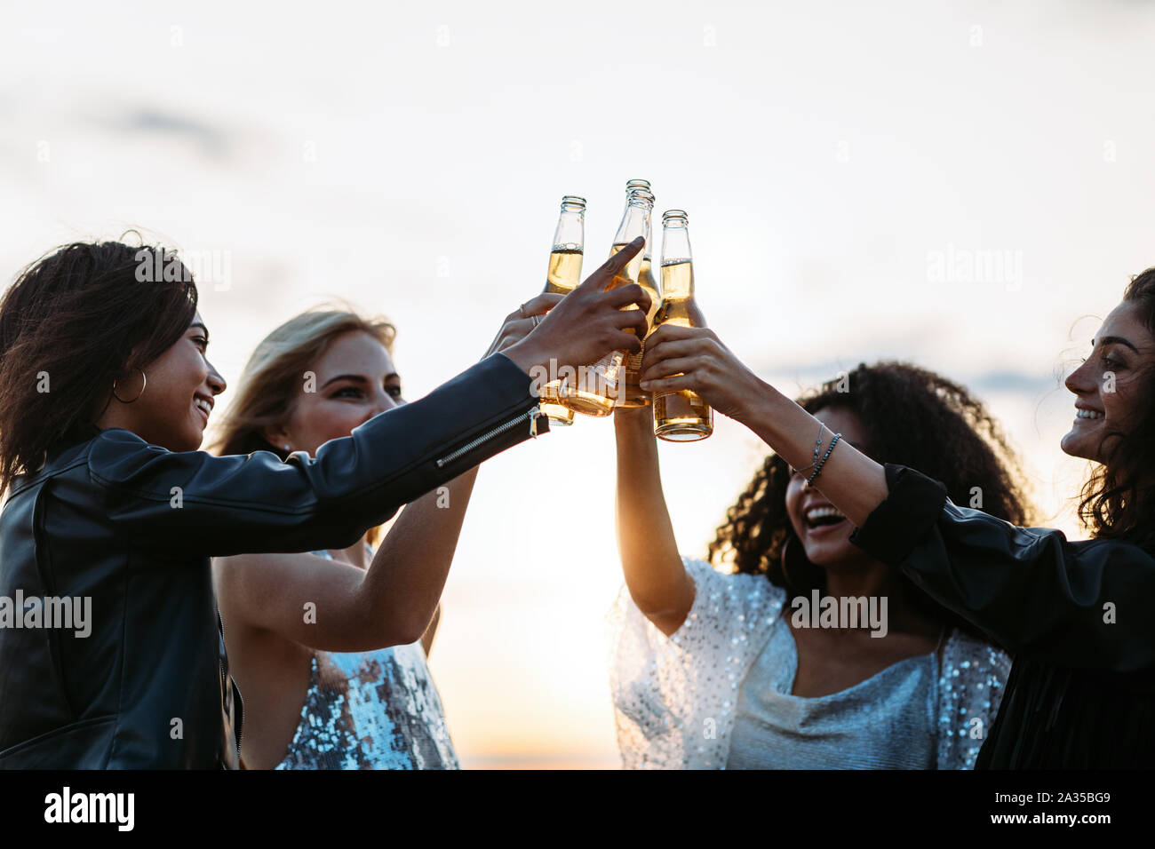 Multi-ethnic friends toasting beers at sunset. Women celebrating with ...
