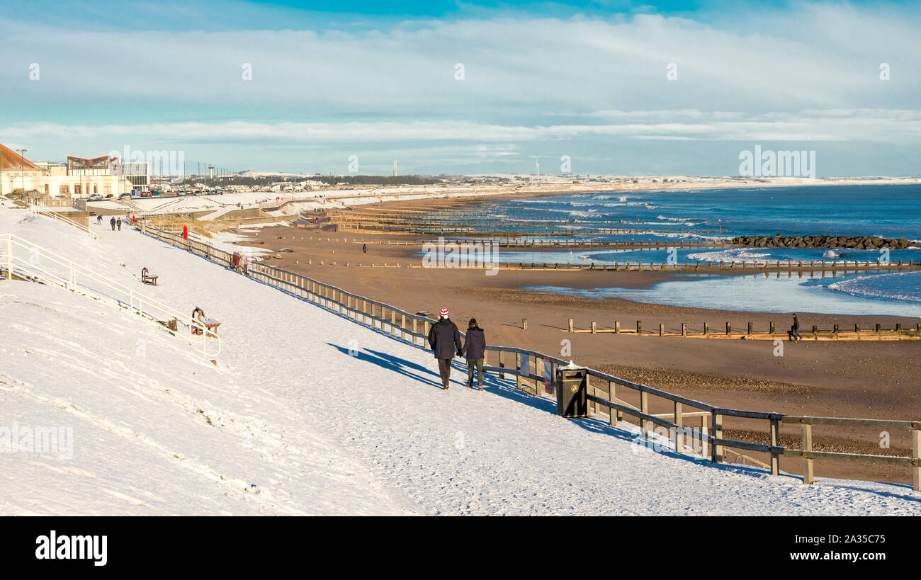 A couple walk on a promenade footpath along the beach in a nice sunny ...
