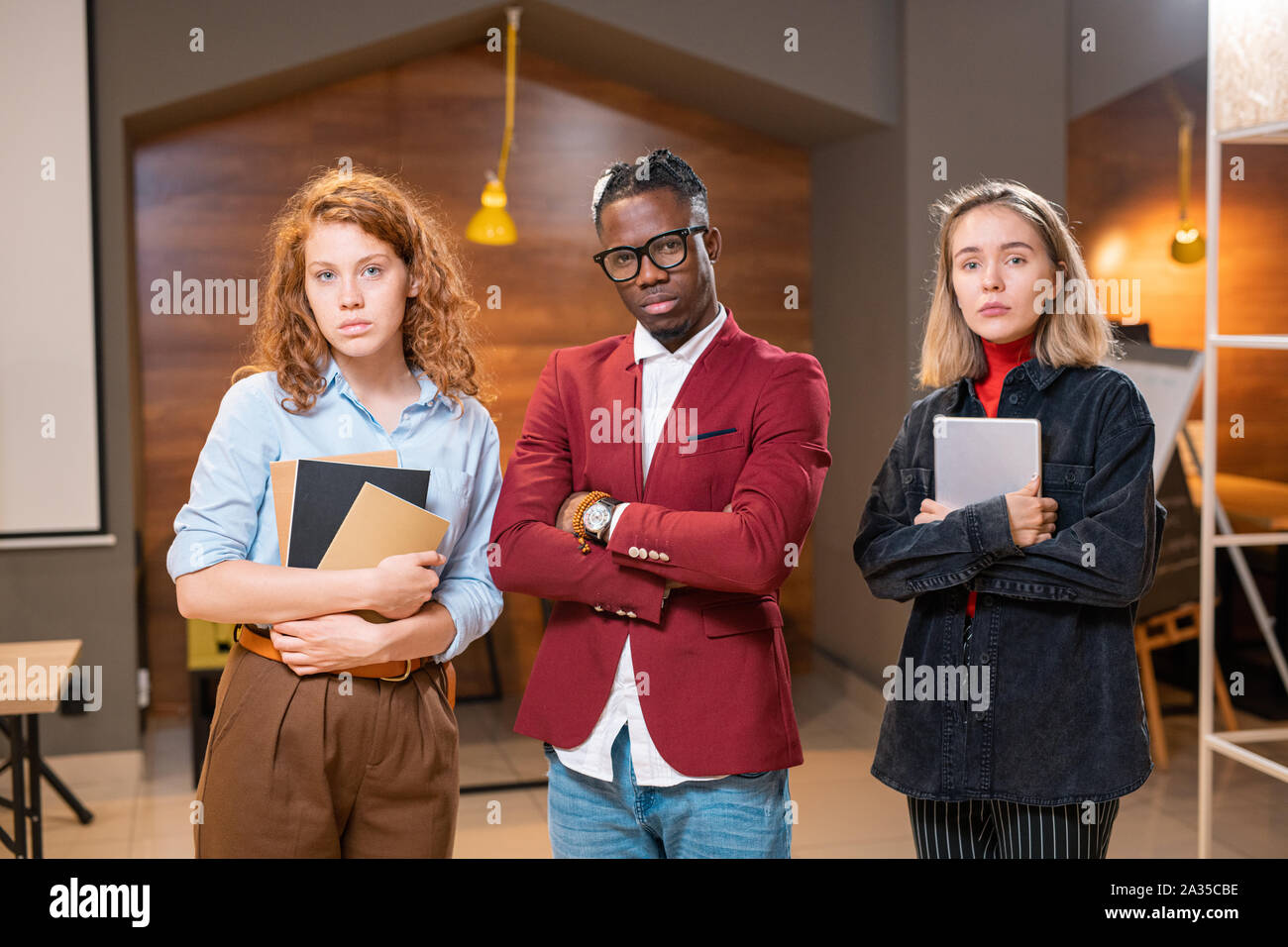 Three young serious multicultural students in casualwear standing in ...
