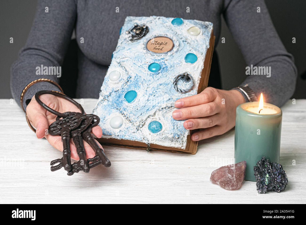 Magician with a book of magic and ancient keys in hand sitting by her ...