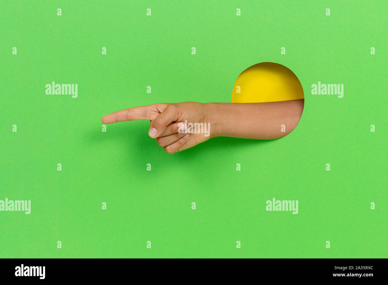 Hand through hole in green background pointing with finger to something ...