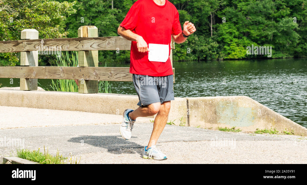 A man is running over a bridge bu a lake during a 10K race in the woods ...