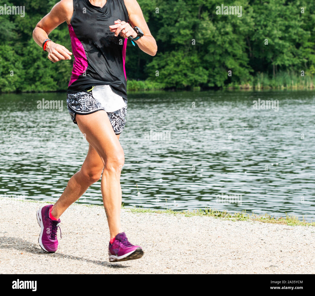 An adult female runner is racing a 10K on a dirt path passing a lake ...