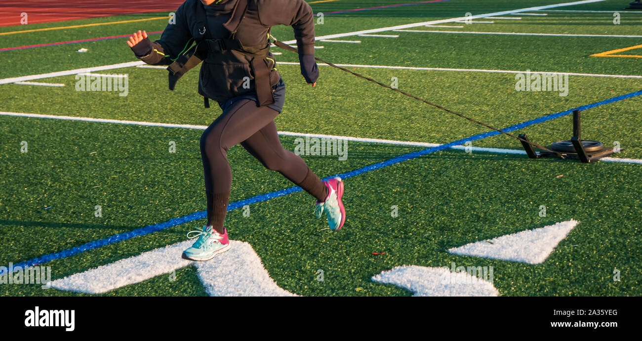 A high school track sprinter is pulling a sled with weights on it ...