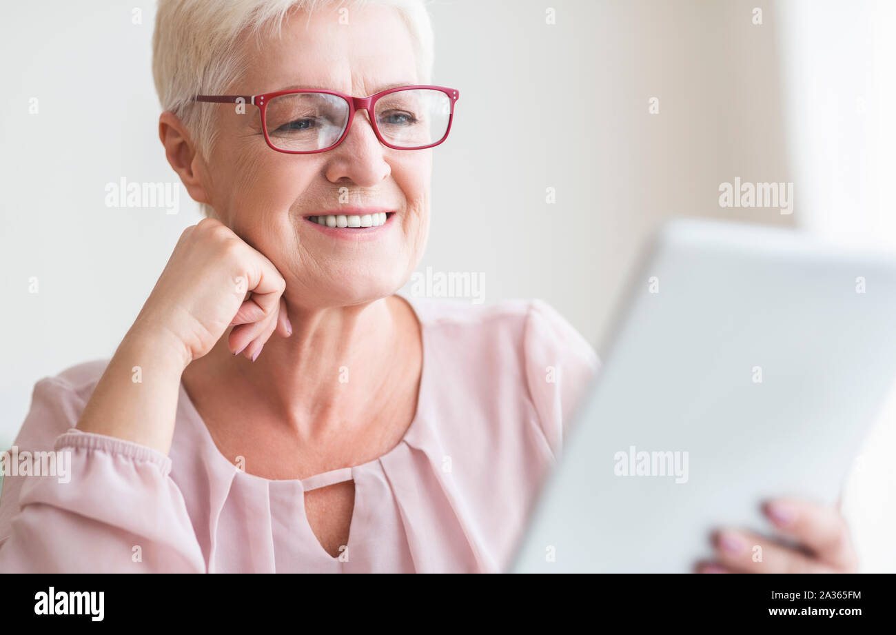 Smiling beautiful senior woman reading book on digital tablet Stock ...