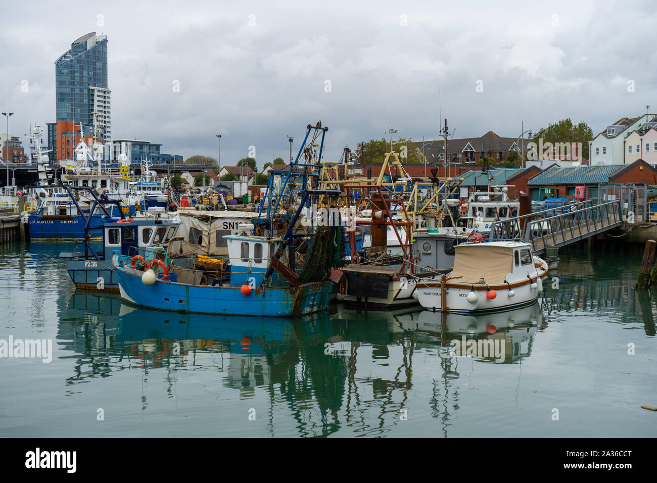 Fishing boats docked in a quay reflecting on calm waters at camber ...