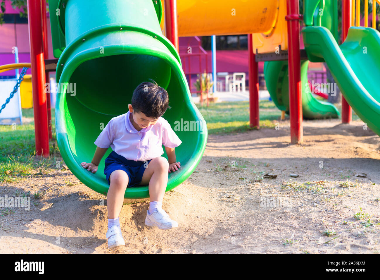 Asian kid playing slide at the playground under the sunlight in summer ...