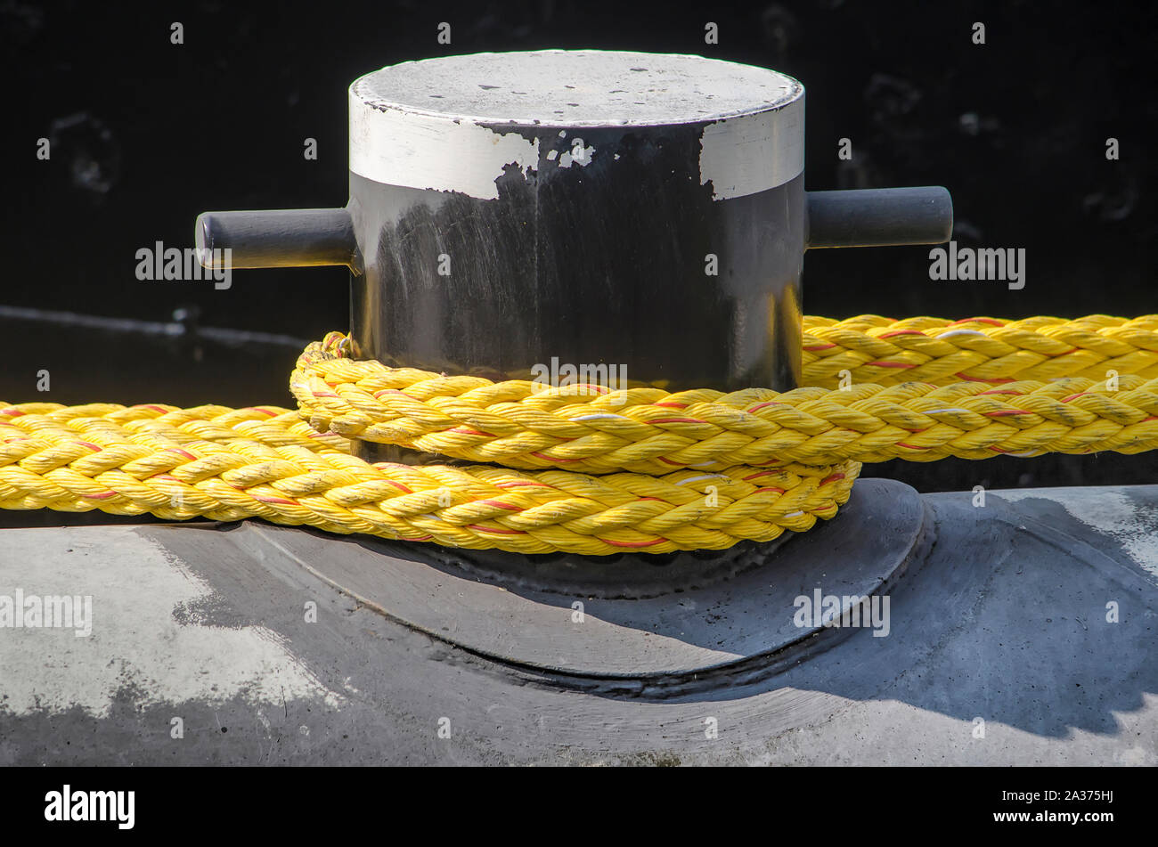 Close-up of thick yellow marine ropes around a black steel bollard ...