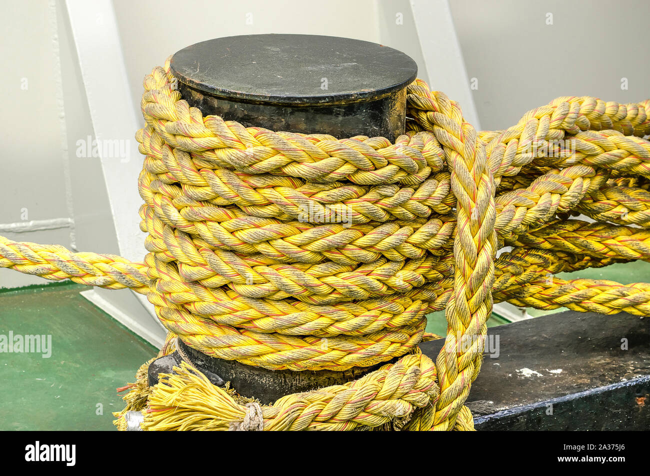 Thick yellow marine rope around a steel bollard on board of a ship ...