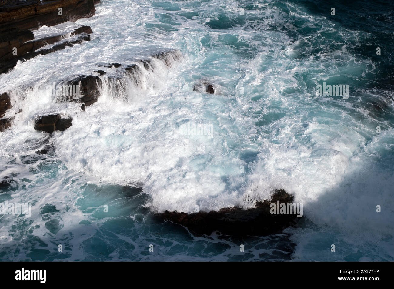 Wave breaking over rocks at bottom of cliff Stock Photo - Alamy