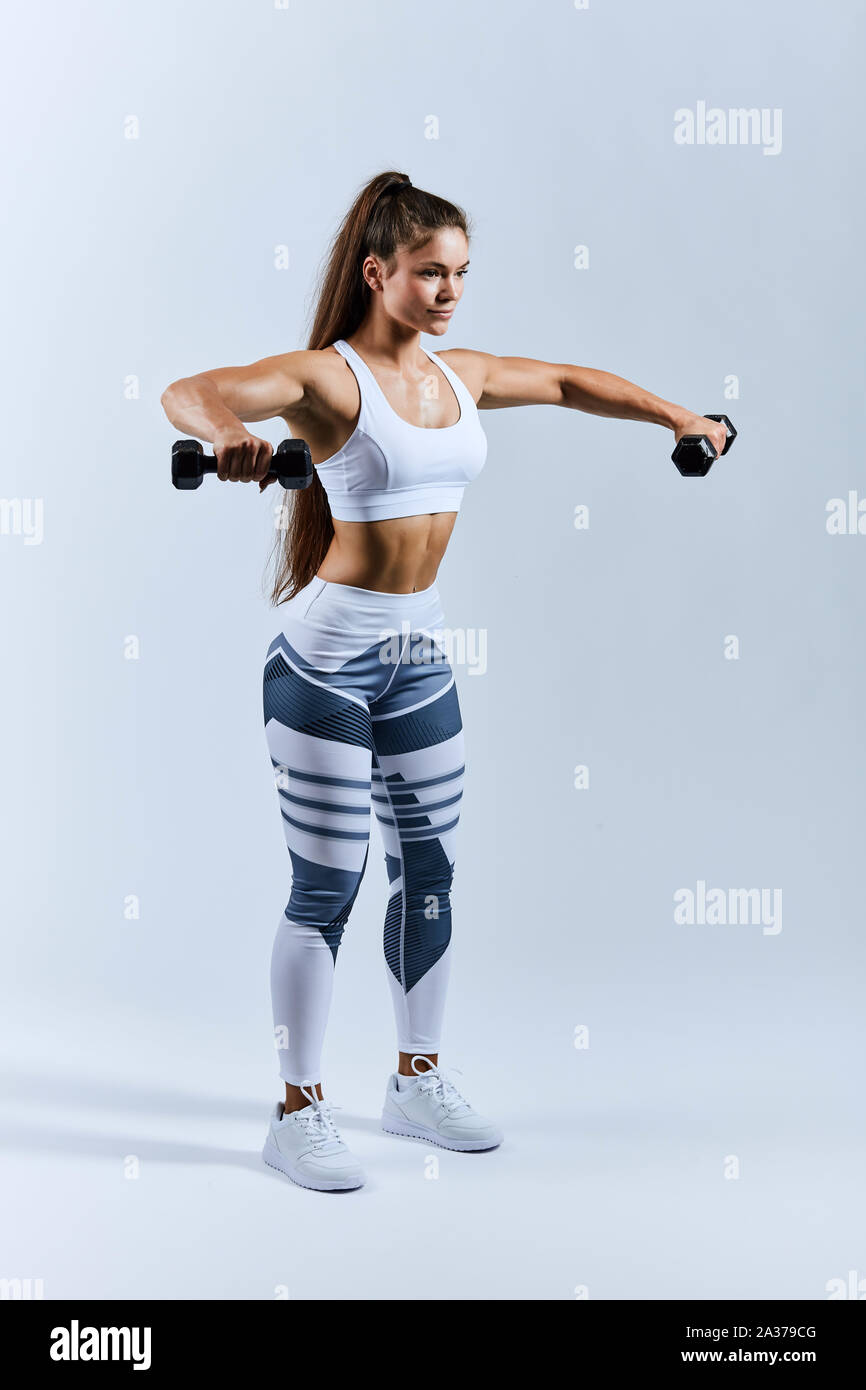 active good looking woman raising dumbbells, trying to keep balance ...