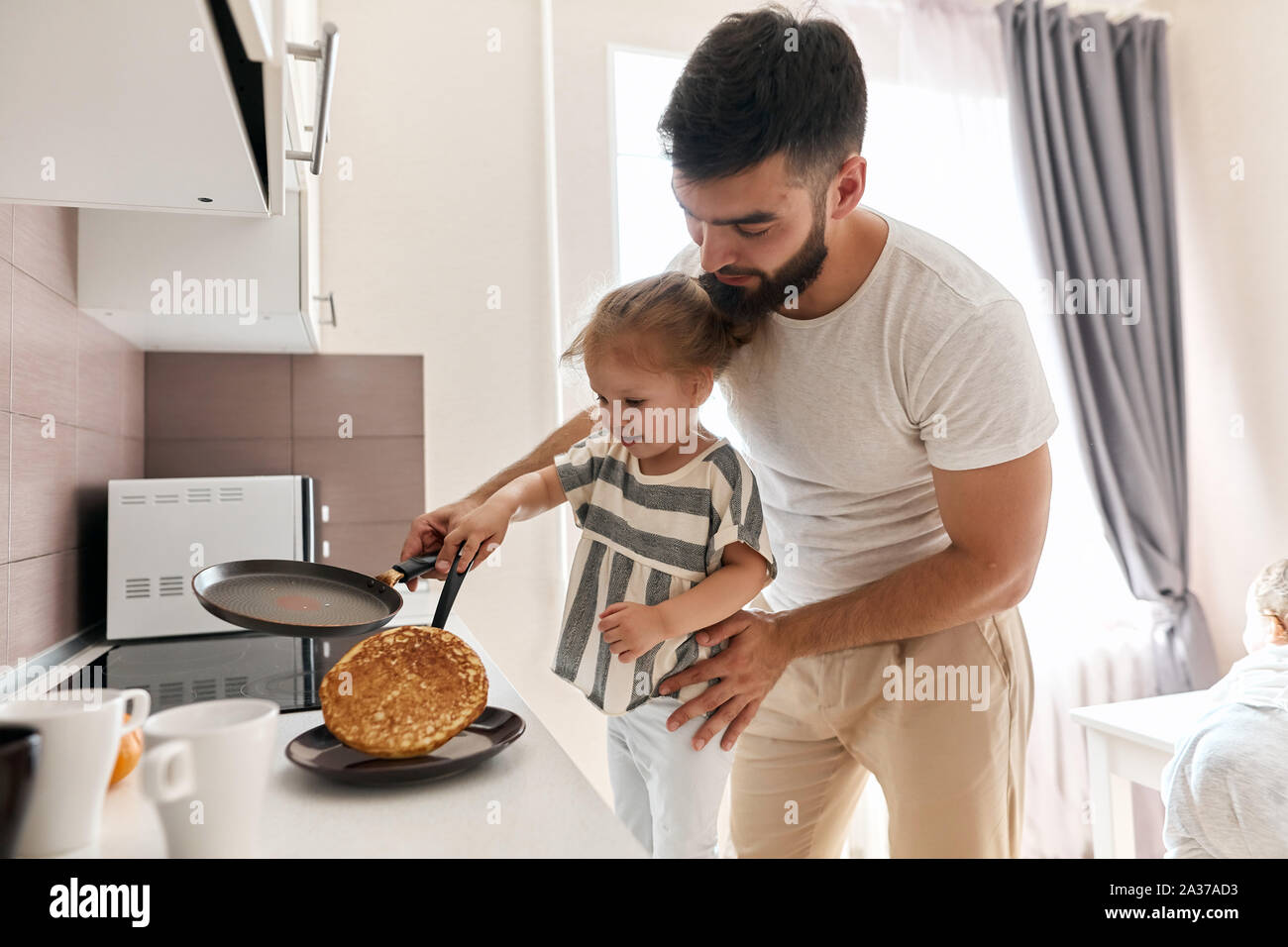 bearded father helping child to turn over the pancake in the kitchen ...