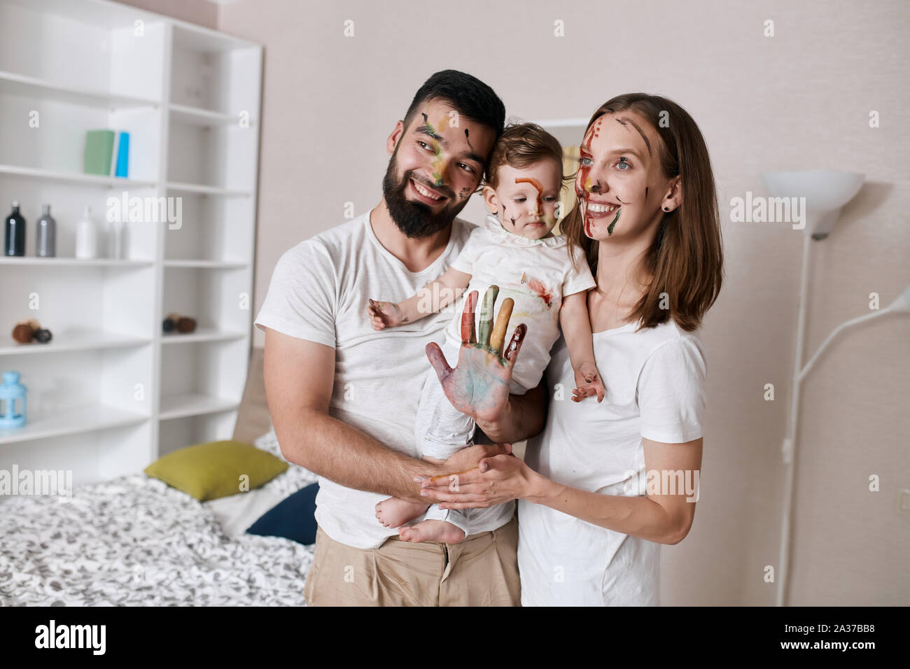 Happy daddy, mommy, kid with paint on faces looking at the camera, art ...