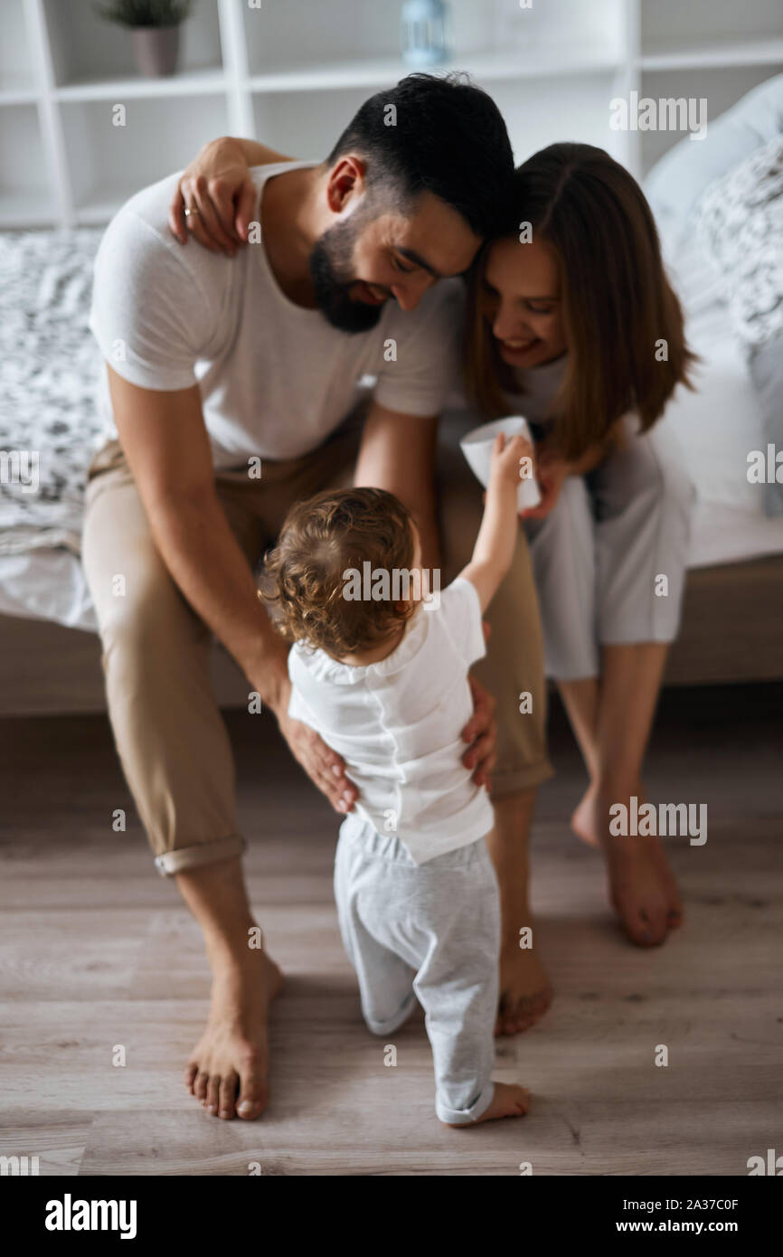 attractive cheerful parents teaching baby to walk, full length photo ...