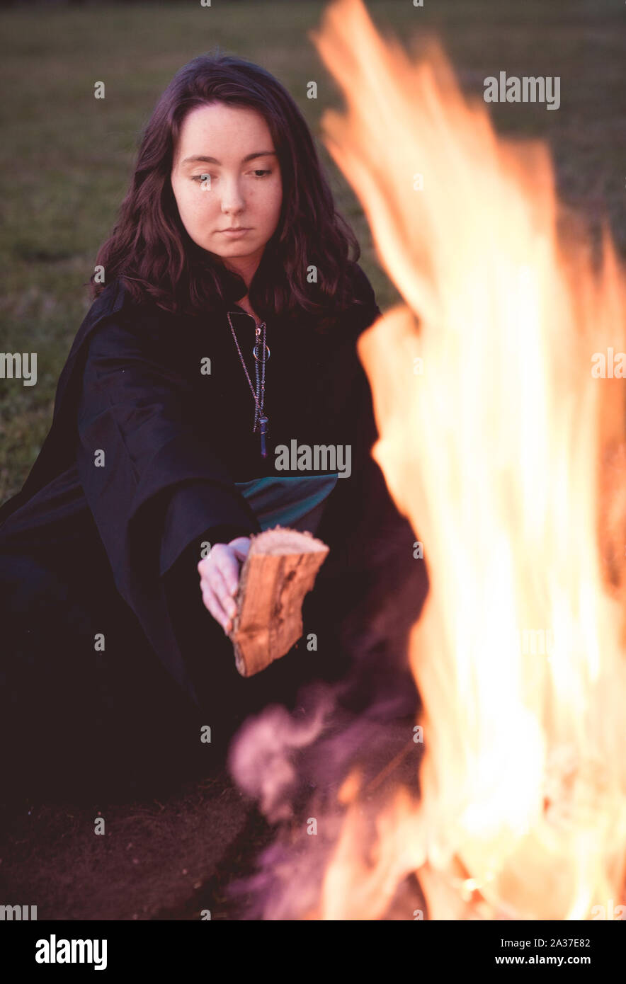 A pretty, teenage girl placing logs on an outdoor camp fire whilst ...