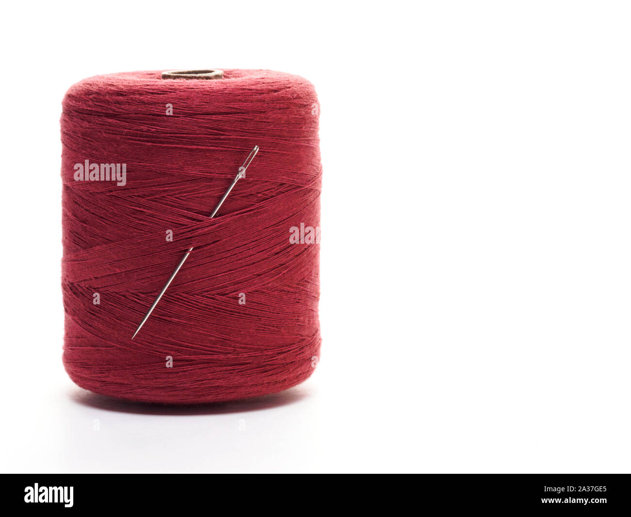 Red spool of thread with needle in a vertical position on a white ...