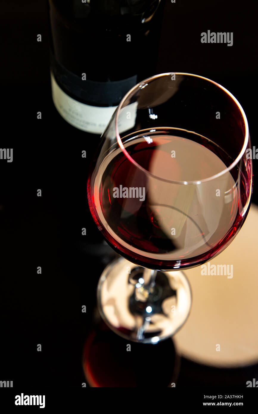 a glass of red wine in top view (focus on margin) with a blurry bottle ...