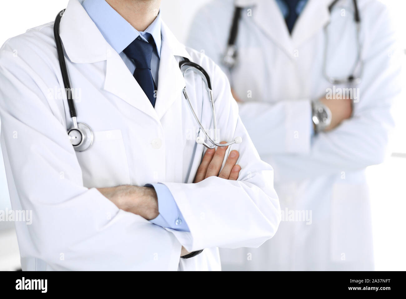 Doctor man standing straight and crossed arms with colleague at ...