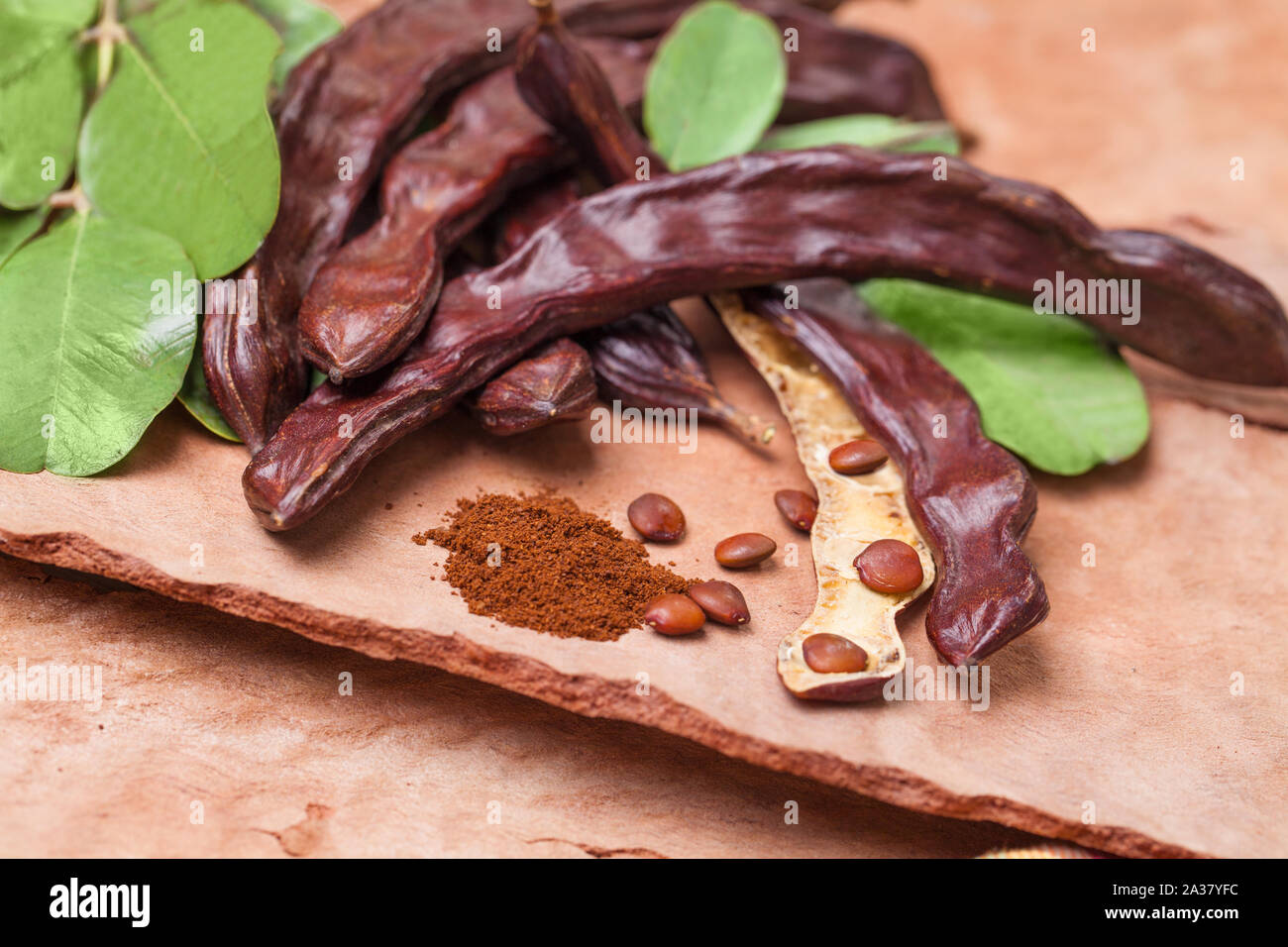 Carob. Organic carob pods with seeds and leaves on tree bark table ...