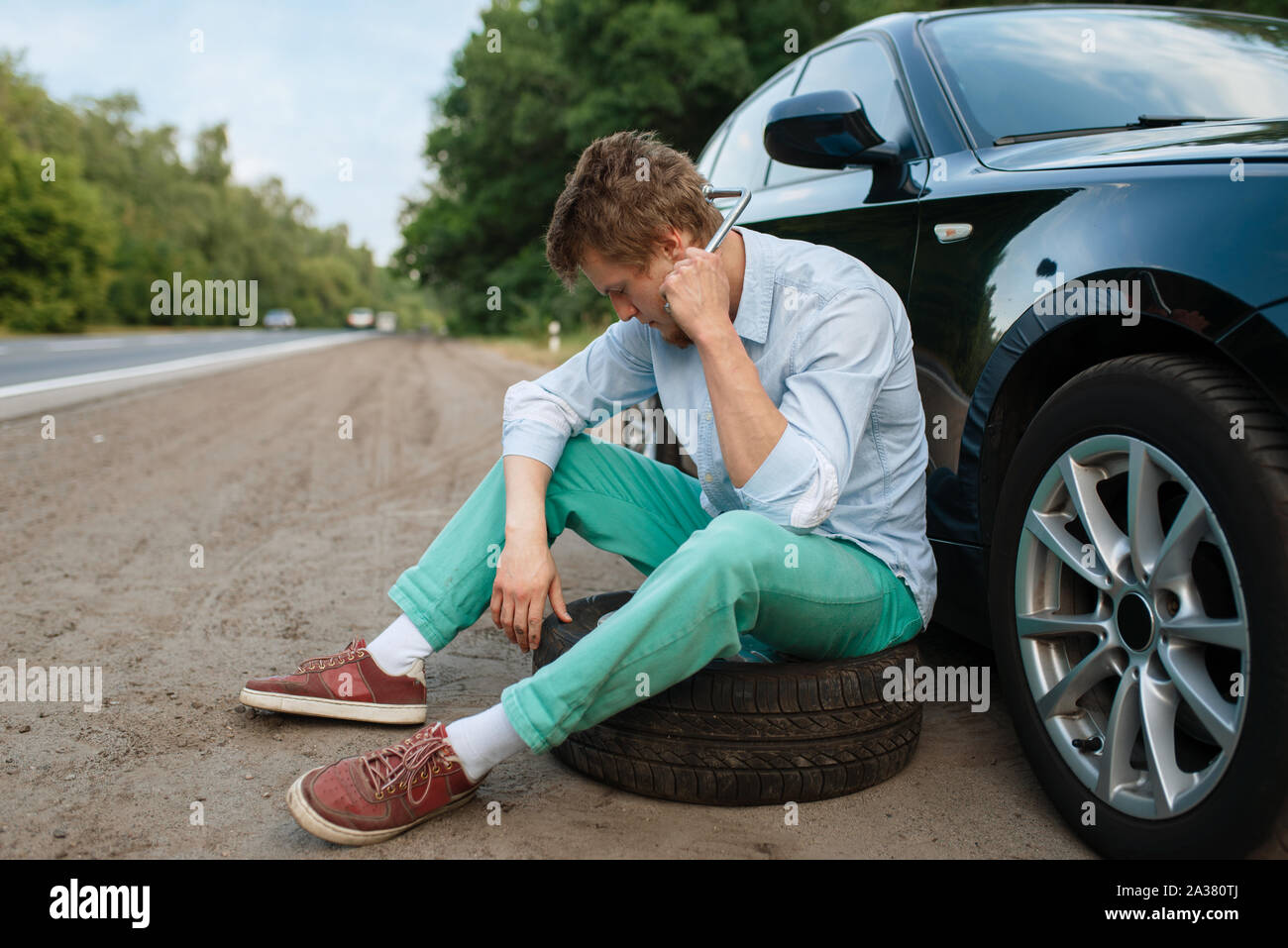 Car breakdown, young man sitting on spare tyre Stock Photo - Alamy