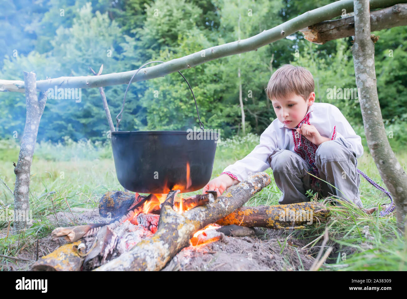 Slavic child in national clothes near the fire. Ukrainian boy in nature ...