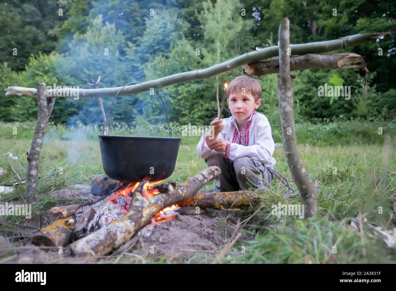Slavic child in national clothes near the fire. Ukrainian boy in nature ...