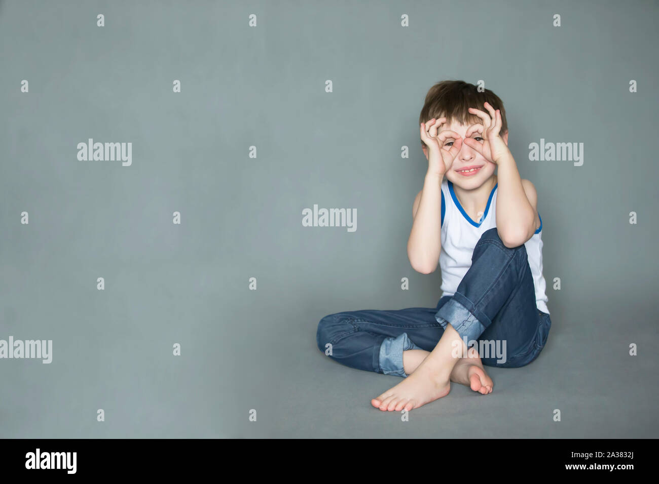 Comic happy boy holding his fingers near the eyes like glasses. Cheerful seven eight year old ...