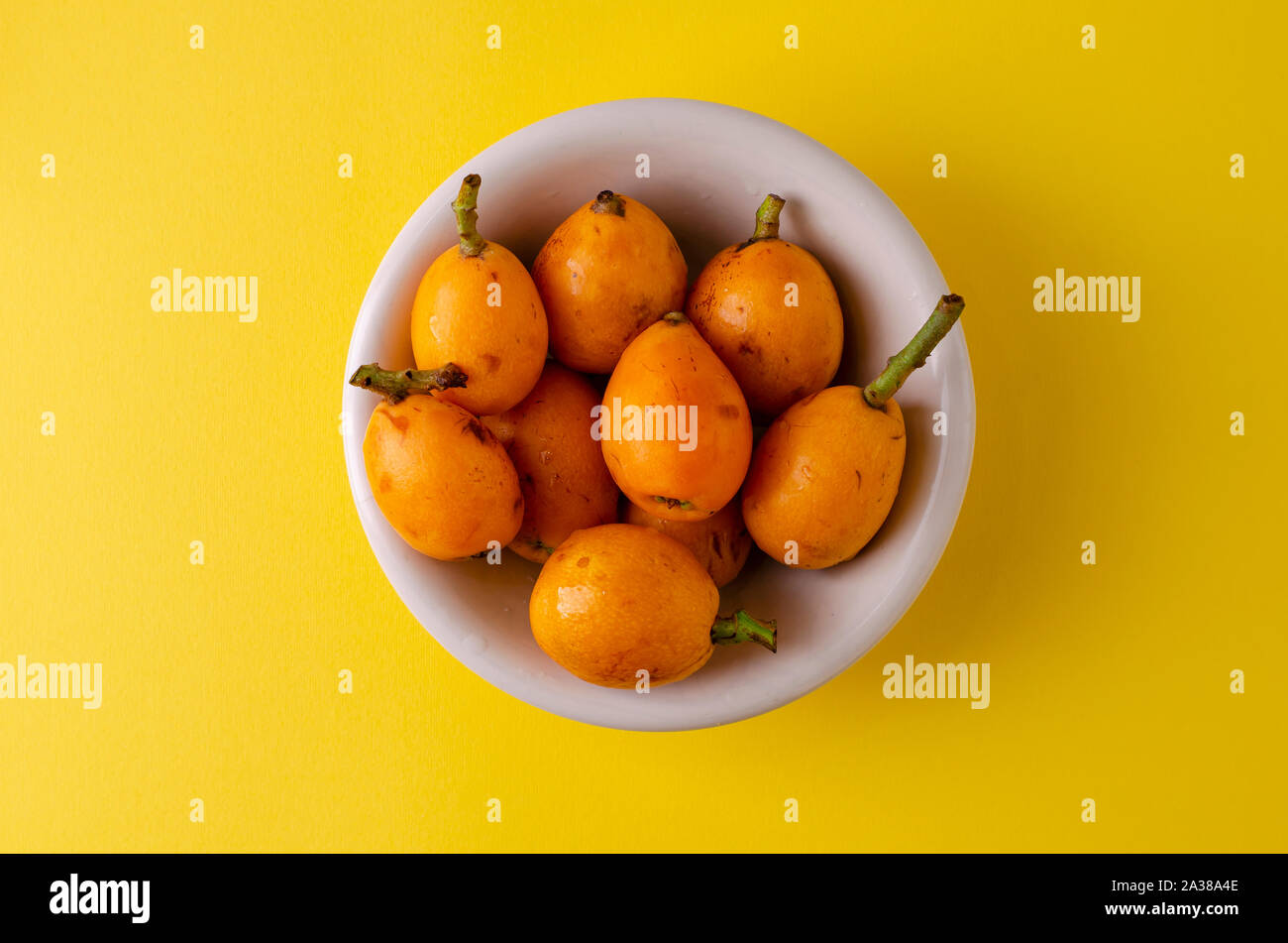 Loquat fruits in a white bowl on bright yellow background with a space ...