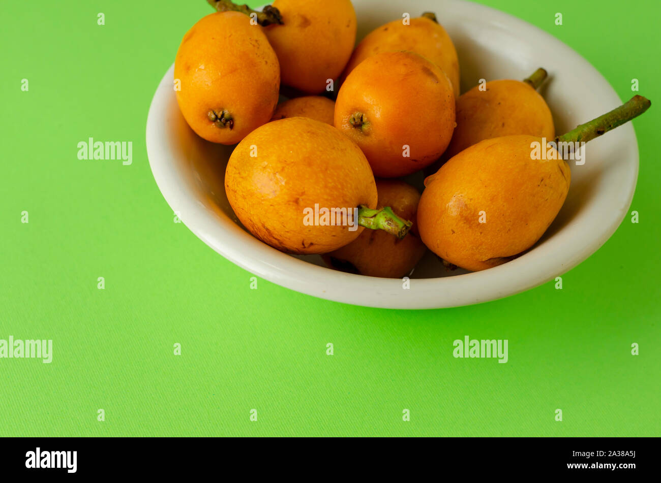 Loquat fruits in a white bowl on bright green background with a space ...