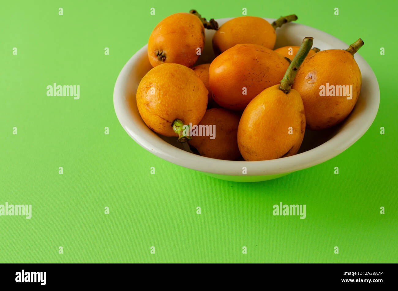 Loquat fruits in a white bowl on bright green background with a space ...