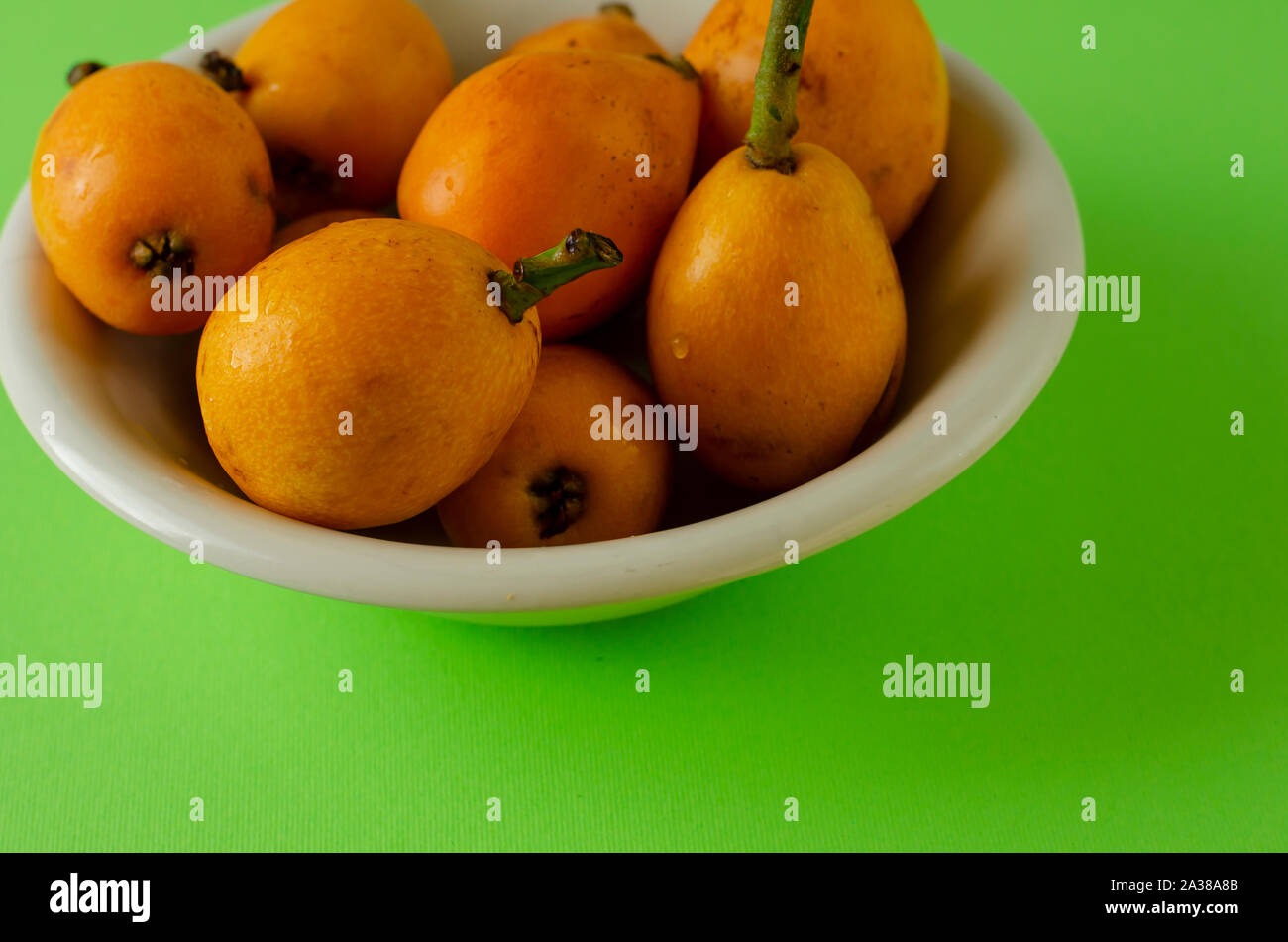 Loquat fruits in a white bowl on bright green background with a space ...