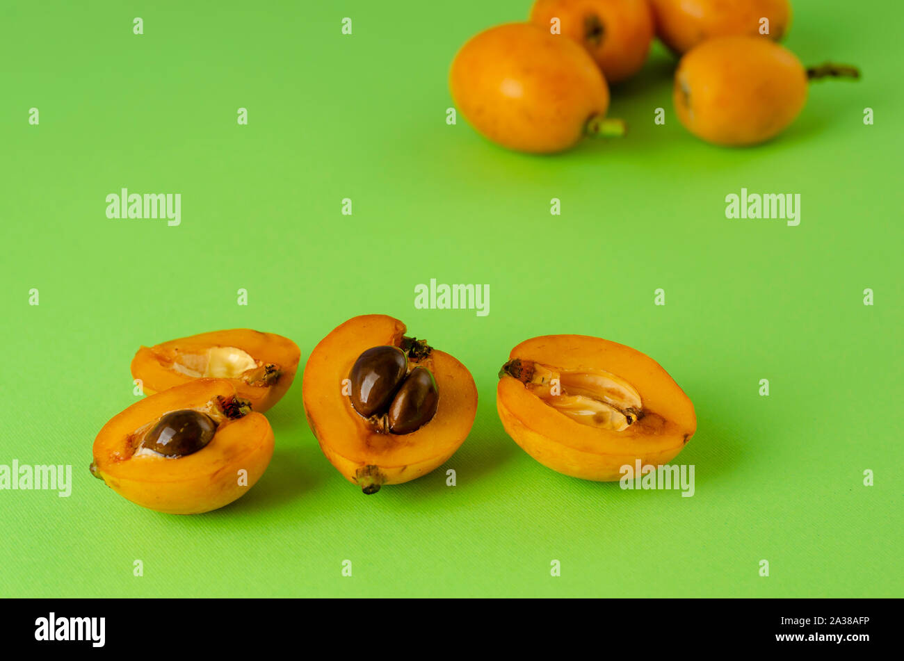 Halves of a Loquat fruits on a bright green background with a space for ...