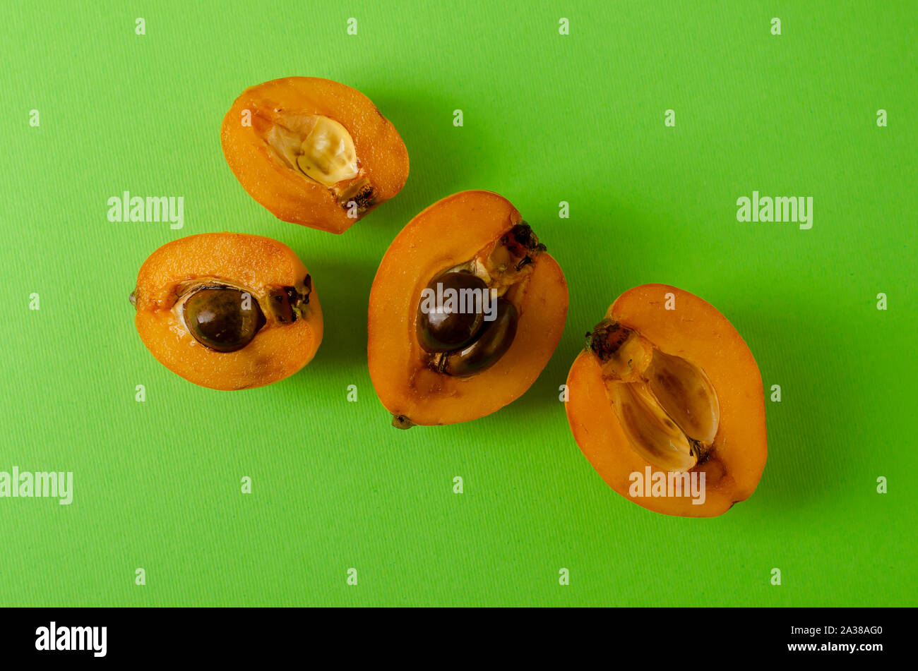 Halves of a Loquat fruits on a bright green background with a space for ...
