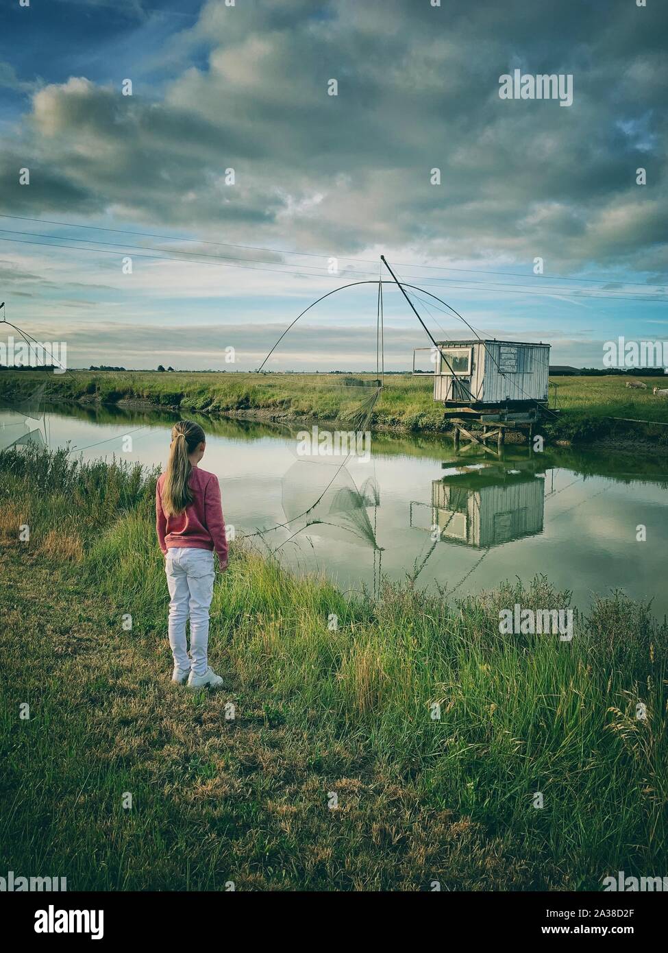 Girl standing by a river looking at fishing huts and nets, Rue Du Gois ...
