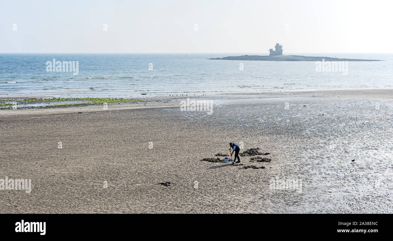 Man digging worms from sand on Douglas Beach, Isle of Man with Tower of ...