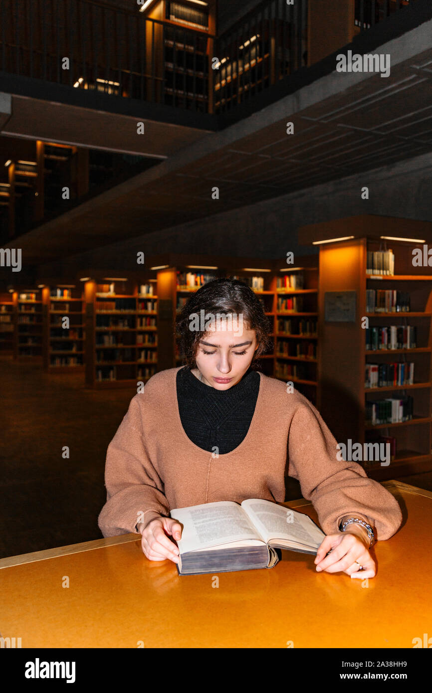 Young brunette girl bent over book sitting in library alone Stock Photo ...